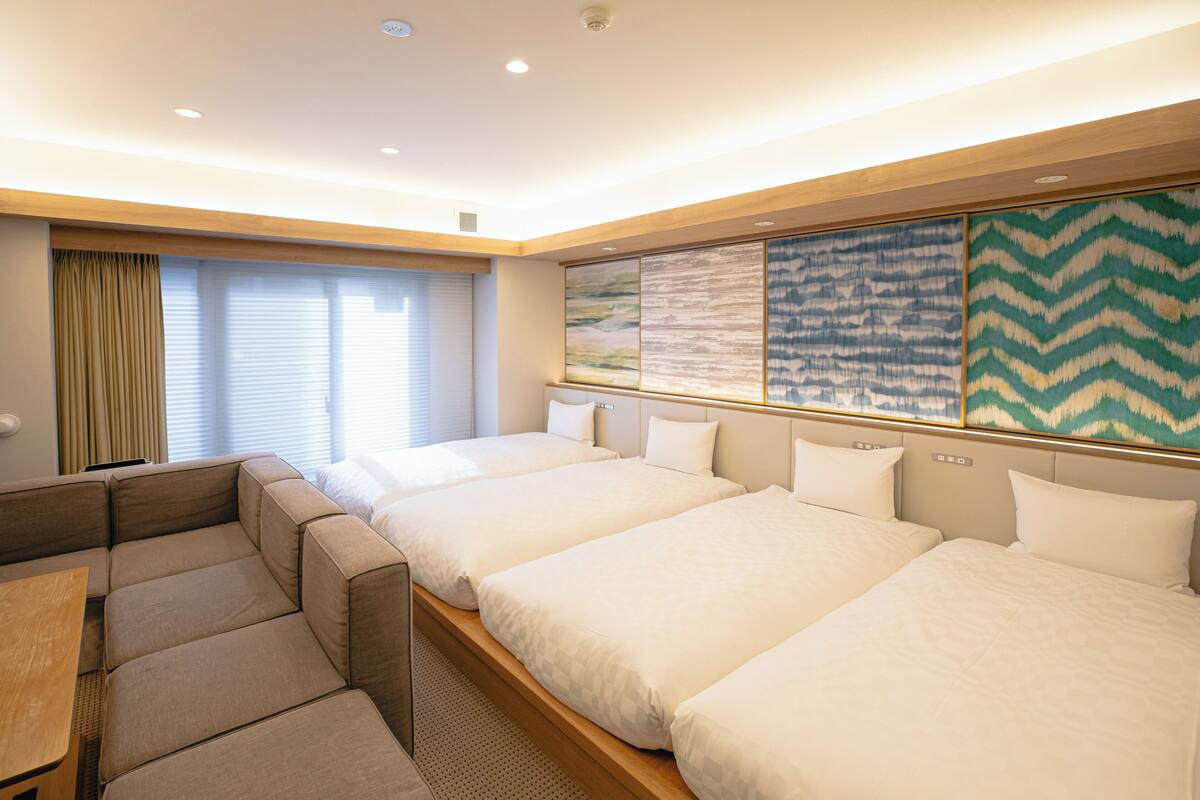 Quarto de hotel com sofá-cama, escrivaninha e duas camas de solteiro.