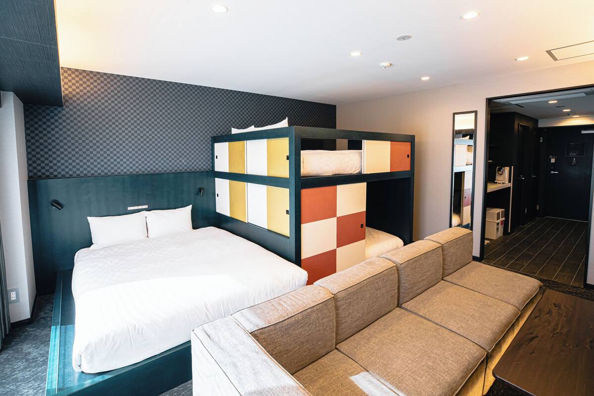 Quarto de hotel com uma cama beliche, um sofá e uma mesa.