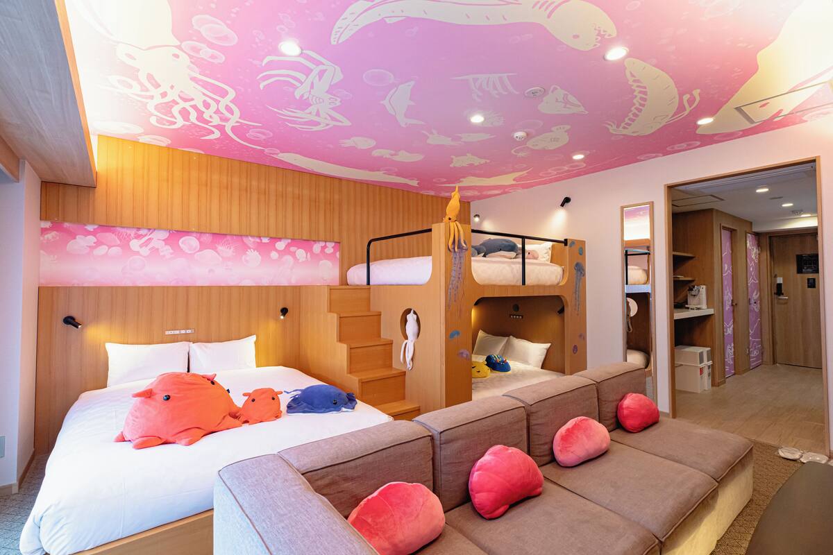 Quarto com beliches, um sofá e um mural no teto.