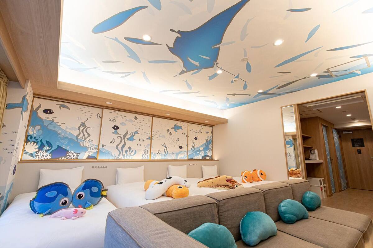 Quarto de hotel com cama, sofá e um mural no teto com peixes.