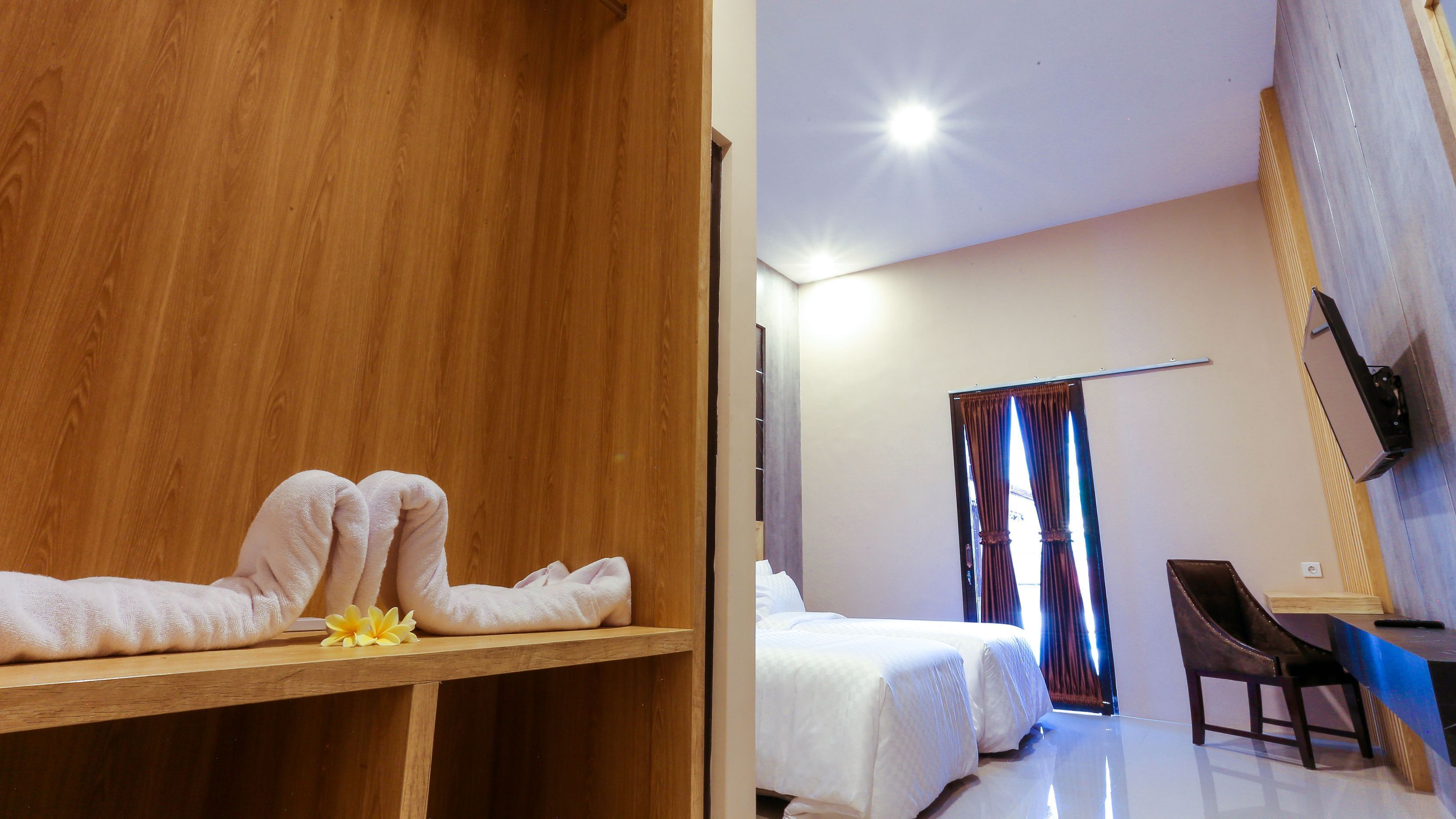 Quarto de hotel com guarda-roupa de madeira, cama com roupa branca, escrivaninha com controle remoto e uma cadeira.