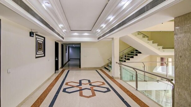 Corredor moderno de hotel com piso estampado em padrão geométrico, escada com guarda-corpo de vidro e teto com iluminação embutida.