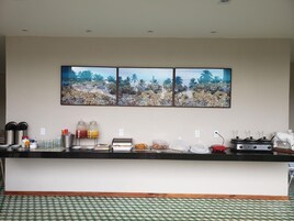 Uma cozinha de hotel com buffet, incluindo estação de café, dispensadores de suco e fogão.