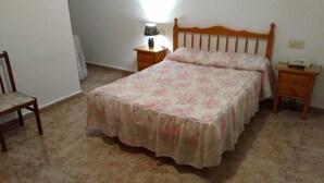 Quarto com cama, mesa de cabeceira, cadeira e abajur.