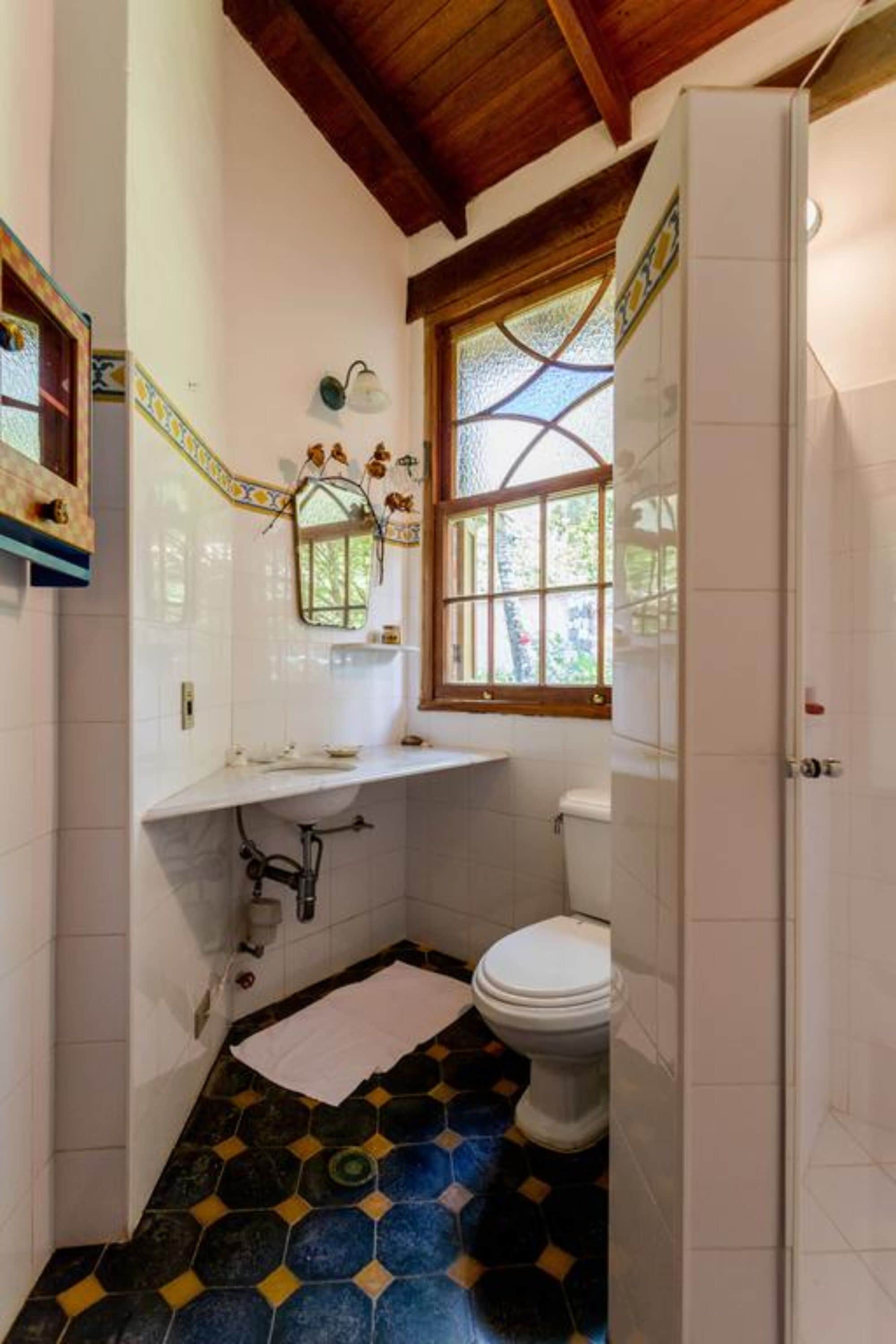 Casa de banho com sanita branca, lavatório com espelho e janela.