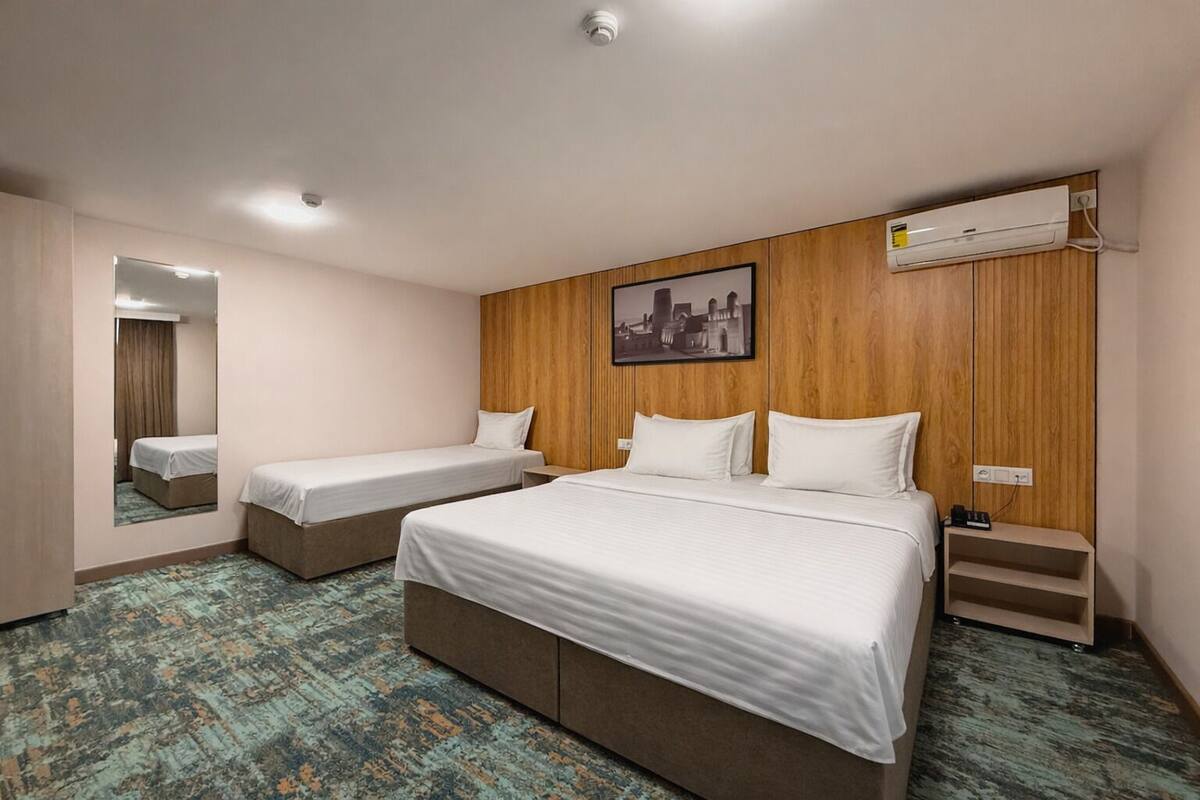 Quarto de hotel com duas camas de solteiro, uma cama grande, cabeceira de madeira, um espelho, ar condicionado e piso coberto por carpete.