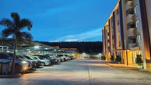 Um estacionamento com carros e um edifício com vários andares e varandas.