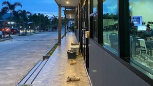 Uma galeria coberta com parede de vidro, mesas ao ar livre e vista para a rua.