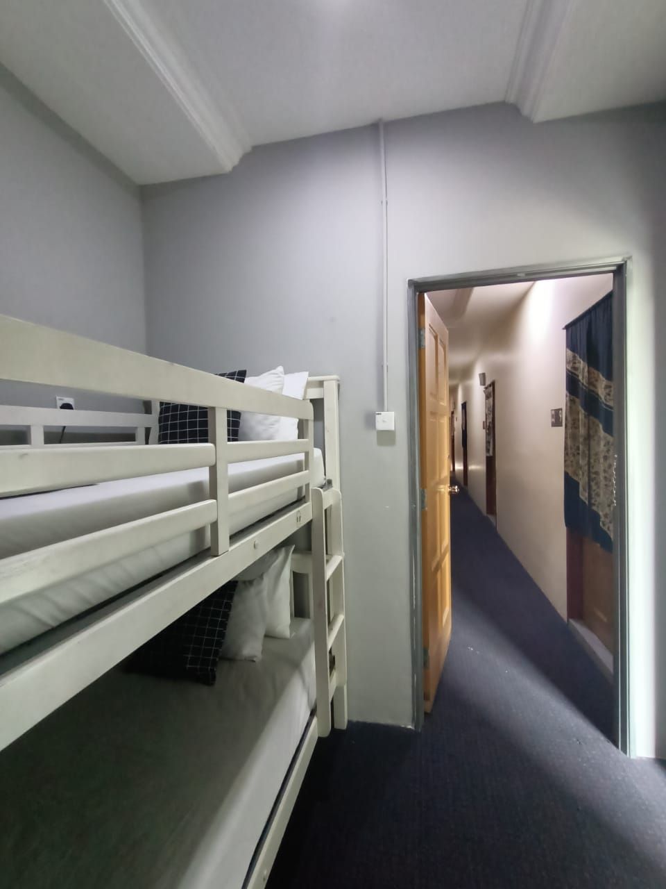Corredor estreito com uma cama beliche à esquerda e uma porta no final.