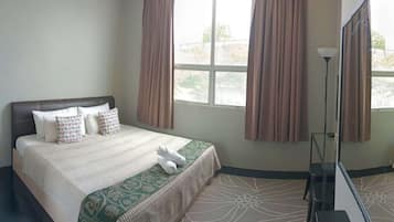 Quarto de hotel com cama, janela com cortinas, luminária e vista para o exterior.