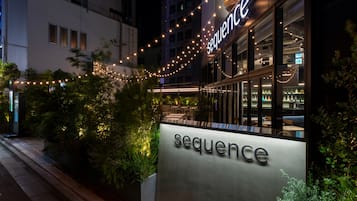 Um edifício com o nome 'Sequence' iluminado na fachada, rodeado por vegetação e luzes de Natal.
