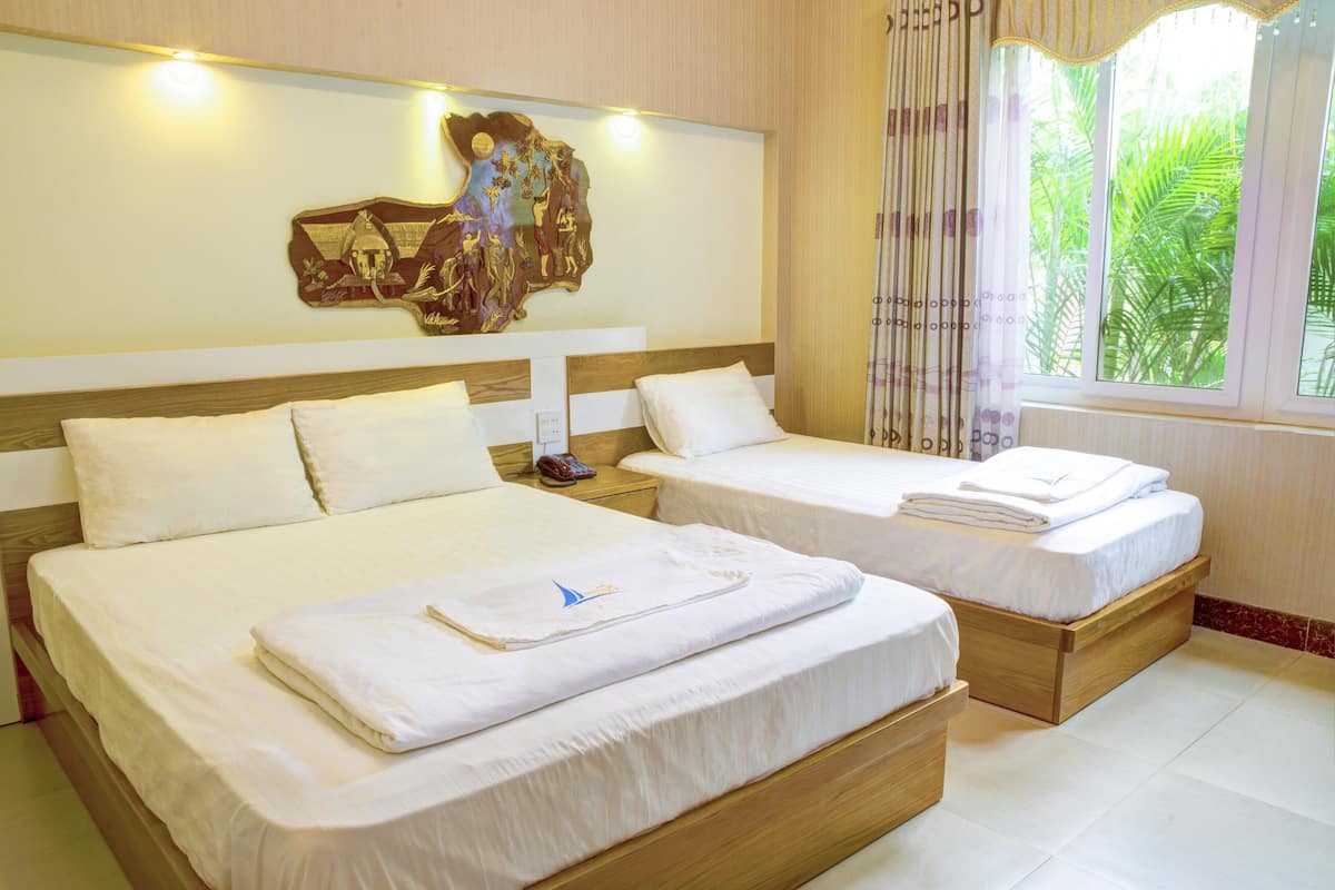 Quarto de hotel com duas camas, um painel decorativo na parede, uma mesa de cabeceira e uma janela com vista para o verde.