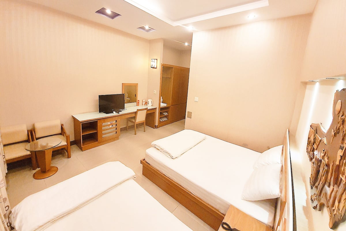 Quarto de hotel com duas camas, uma escrivaninha com computador, uma cadeira, um armário e um espelho.