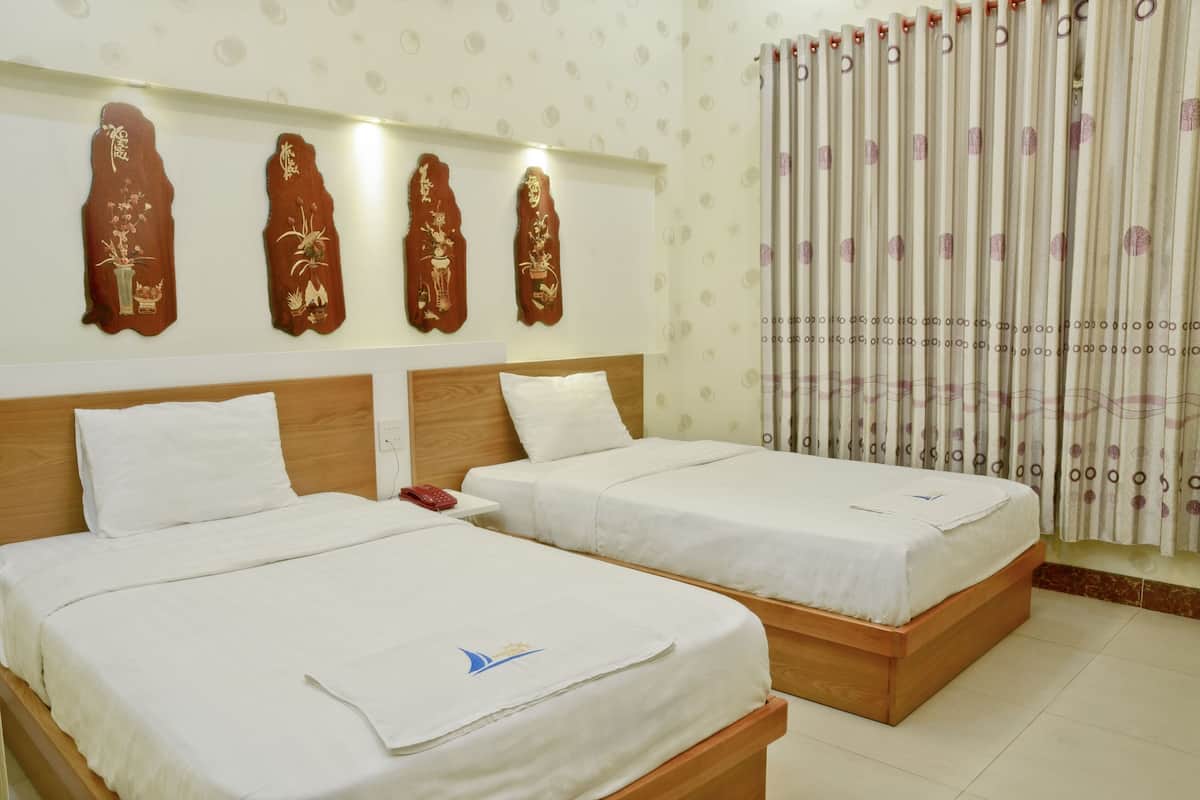 Quarto de hotel com duas camas, cabeceira de madeira, relógio fixado na parede e cortina com padrão circular.