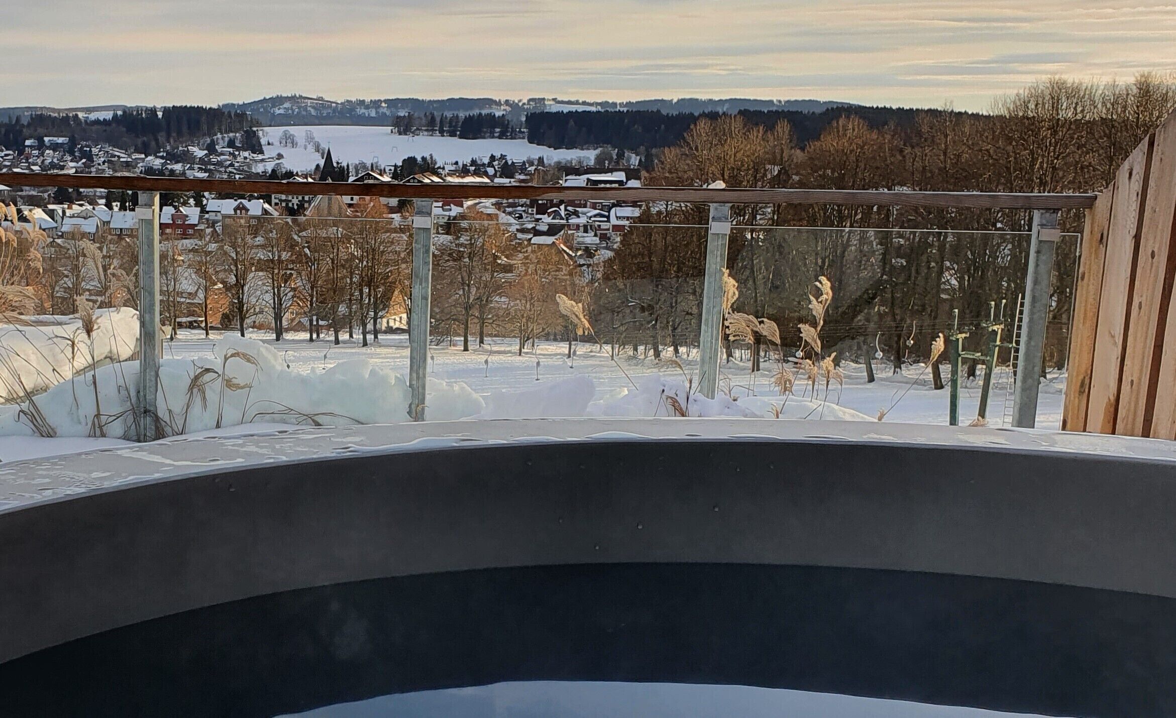 Paisagem coberta de neve com vista para uma aldeia e colinas ao longe.