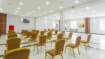 Uma sala de conferências com fileiras de cadeiras, uma TV na parede e um quadro na parede.