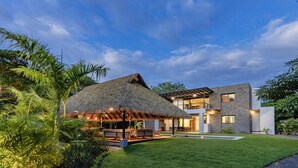 Uma casa moderna com estrutura de colmo e fachada de pedra, cercada por vegetação exuberante.