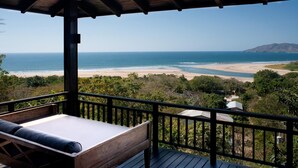 Um deck de madeira com uma cama e vista para a praia e oceano.