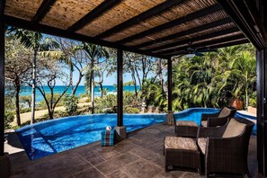 Uma área de piscina coberta com vista para o oceano, rodeada por vegetação tropical.