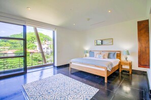 Quarto com uma cama grande, duas mesas de cabeceira, um criado-mudo, janela com vista para o verde e uma luminária no teto.