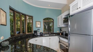 Cozinha moderna com bancada de granito curva, eletrodomésticos de aço inoxidável e grandes janelas com vista para o verde.