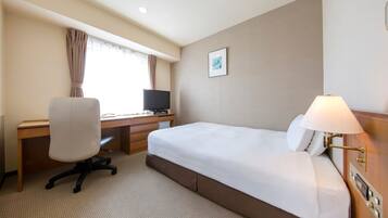 Quarto de hotel com cama, escrivaninha, cadeira, televisão e abajur.