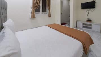Um quarto com cama, cortinas, uma TV fixada na parede e um pequeno armário branco.