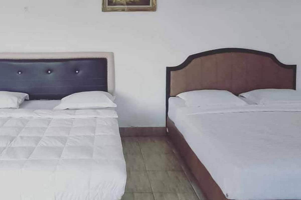 Quarto com duas camas, cada uma com cabeceira de madeira e roupa de cama branca.