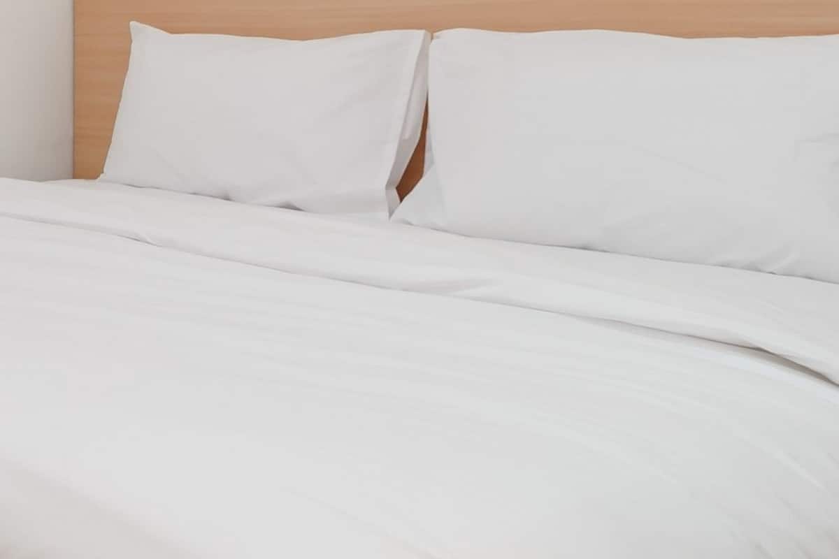 Cama com roupa de cama branca e cabeceira de madeira.
