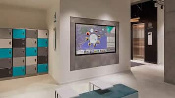 Um hall de hotel moderno com armários, uma tela digital grande e uma área de estar.
