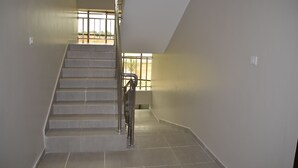 Uma escadaria com corrimão de metal, que leva a um patamar com janelas amplas.