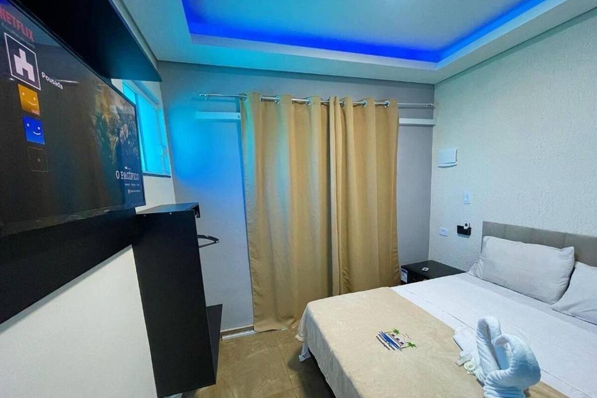 Quarto de hotel com cama, escrivaninha, televisão e cortinas.