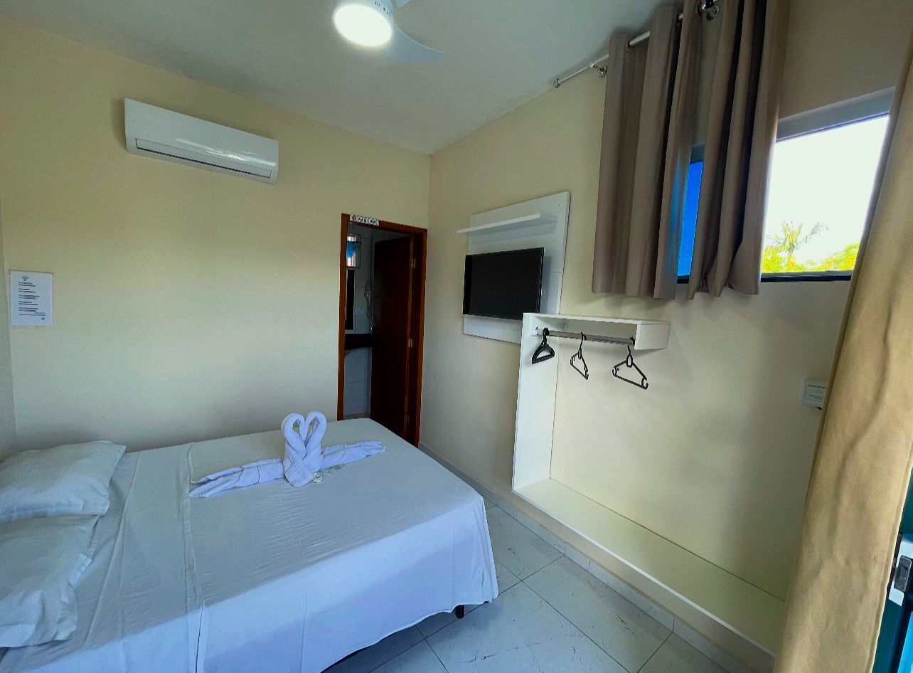 Quarto de hotel com cama, ar condicionado, televisão e janela com cortinas.