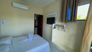 Quarto de hotel com cama, ar condicionado, televisão e janela com cortinas.
