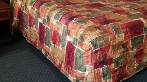 Quarto de hotel com uma cama grande, uma mesinha de cabeceira e uma luminária fixada na parede.