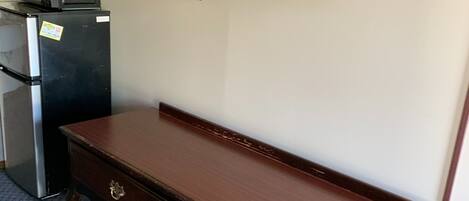 Quarto com cômoda de madeira, televisão de tela plana na parede, geladeira e micro-ondas.