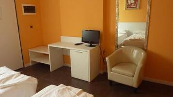 Quarto de hotel com uma cama de solteiro, uma escrivaninha com computador, uma cadeira e um espelho na parede.