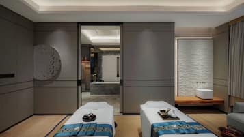 Quarto de hotel moderno com duas macas de massagem, um espelho grande, parede de pedra e pia com cuba branca.