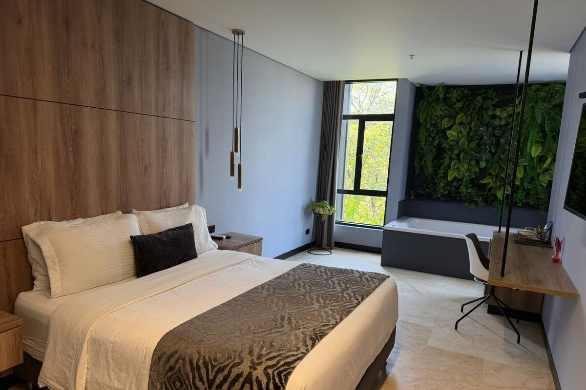 Quarto moderno com cama, mesa de cabeceira e uma janela grande com vista para o verde.