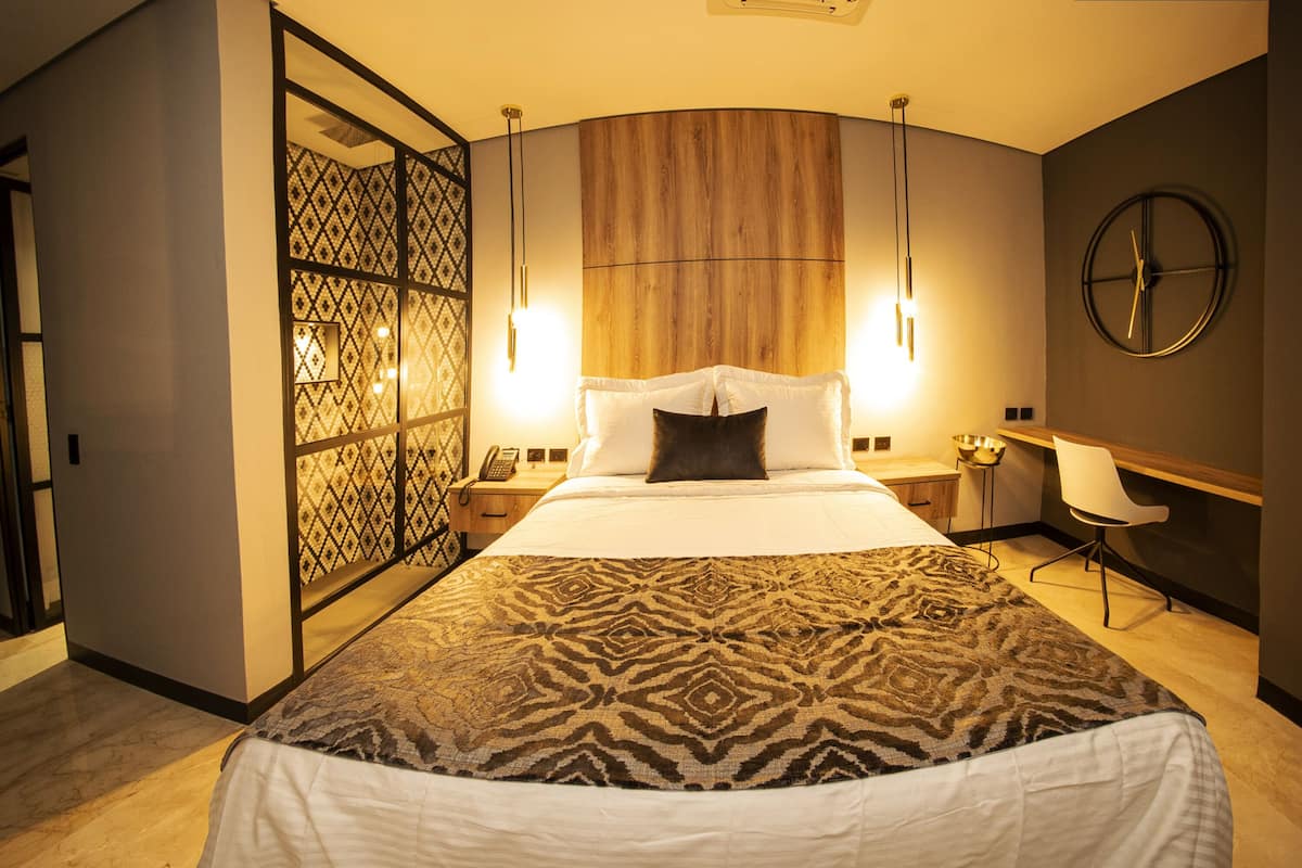 Quarto de hotel com uma cama grande, uma escrivaninha, uma cadeira e um relógio de parede.