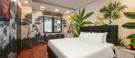 Quarto com uma cama grande, uma mesa de cabeceira, TV na parede e janela com vista para edifícios.