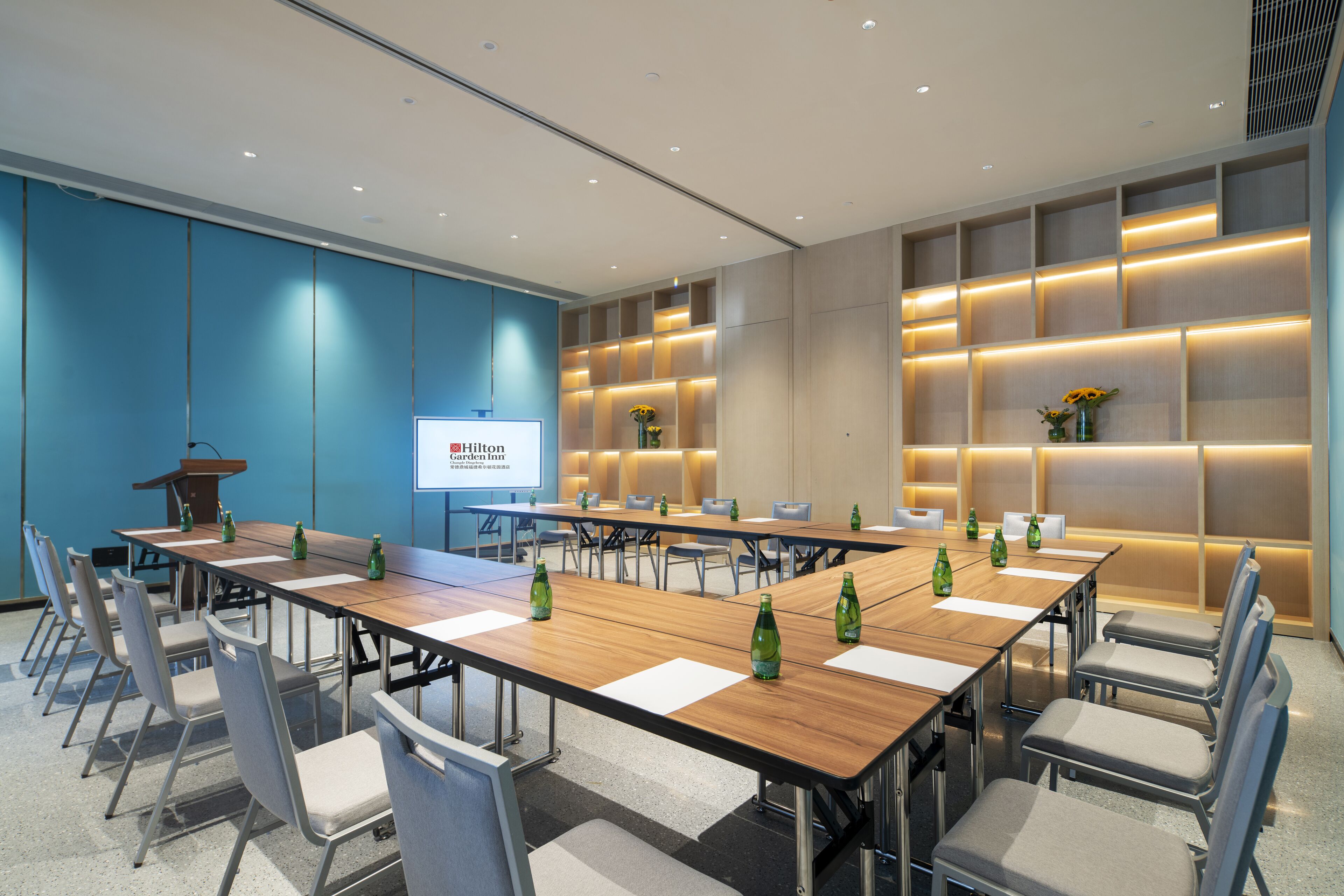 Uma sala de conferência com uma mesa comprida, cadeiras, um pódio e uma tela de apresentação.