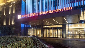 Exterior de um hotel Hilton Garden Inn com design moderno, apresentando uma grande placa iluminada e uma entrada bem iluminada.