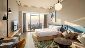 Quarto de hotel moderno com uma cama grande, um sofá, uma escrivaninha e vista para a cidade.