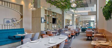 Um restaurante moderno com uma mesa comunitária grande, mesas individuais e um sofá azul.