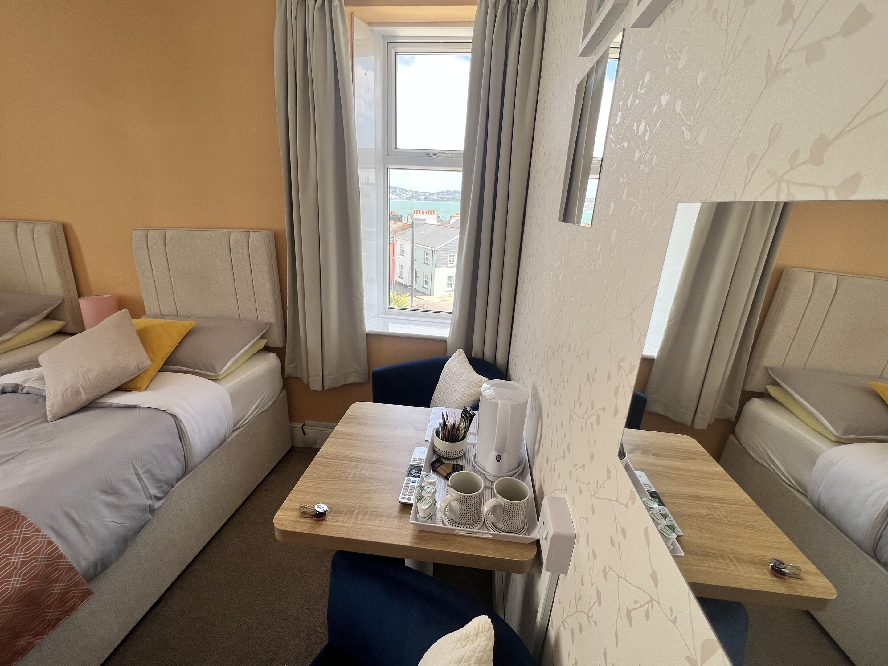 Quarto de hotel com cama, uma mesinha com um serviço de itens, uma cadeira e vista da cidade pela janela.