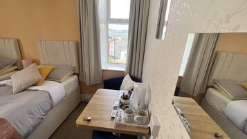 Quarto de hotel com cama, uma mesinha com um serviço de itens, uma cadeira e vista da cidade pela janela.