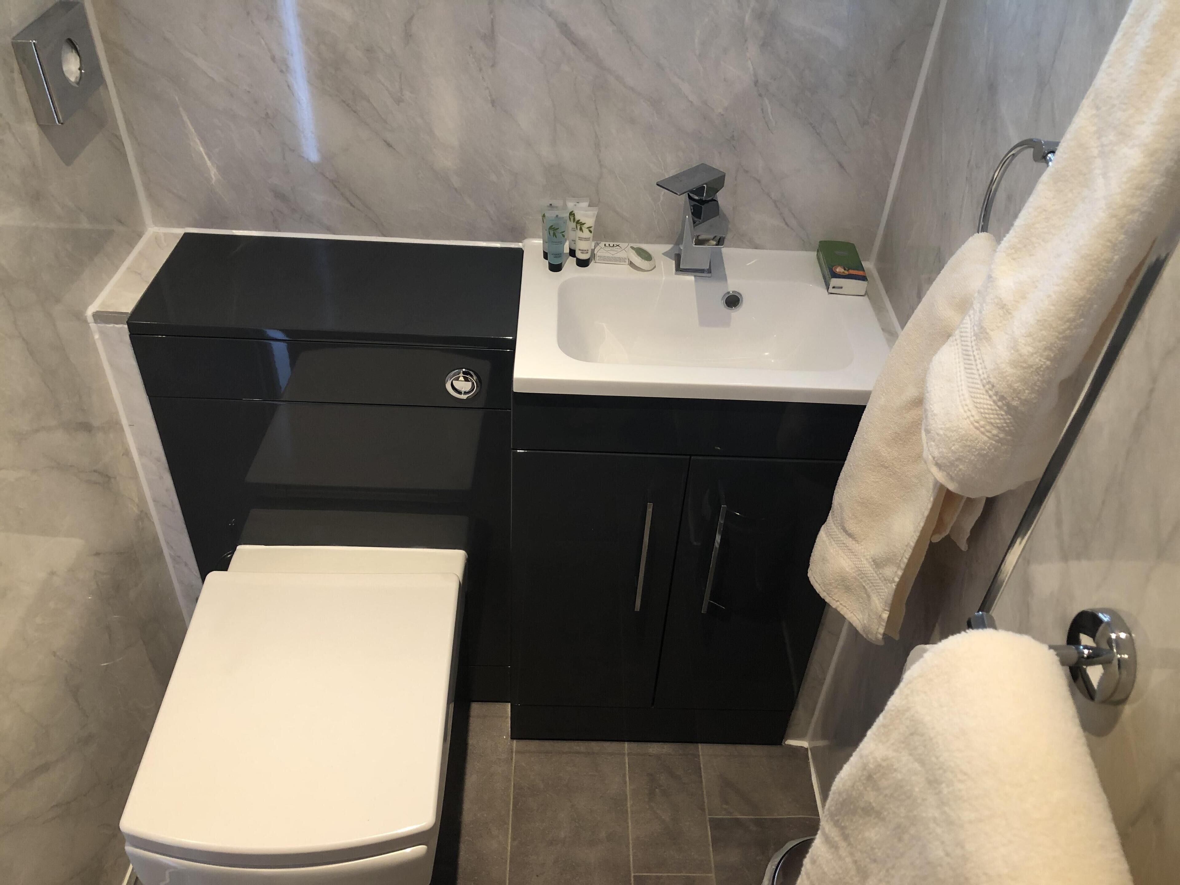 Casa de banho compacta com sanita branca, armários pretos, lavatório com artigos de higiene e um porta-toalhas.