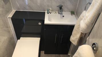 Casa de banho compacta com sanita branca, armários pretos, lavatório com artigos de higiene e um porta-toalhas.