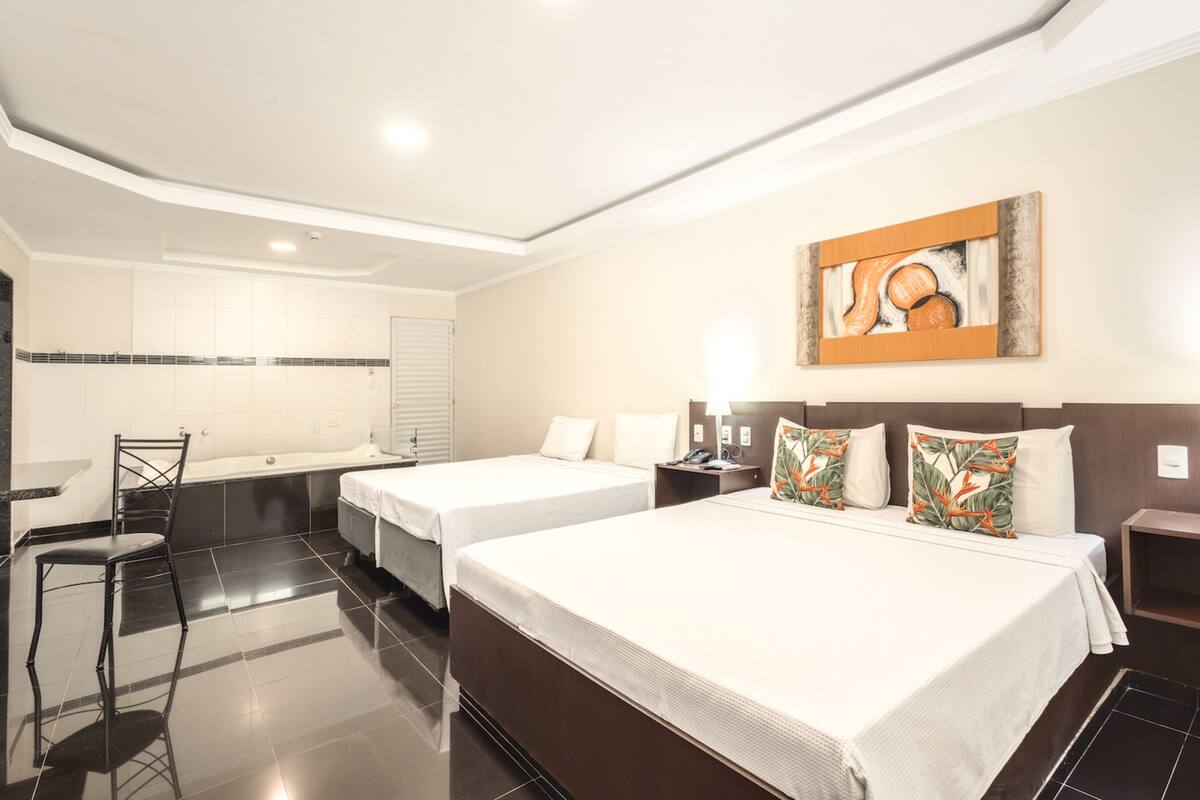 Quarto de hotel com duas camas, área de estar com uma poltrona, banheira e um quadro na parede.